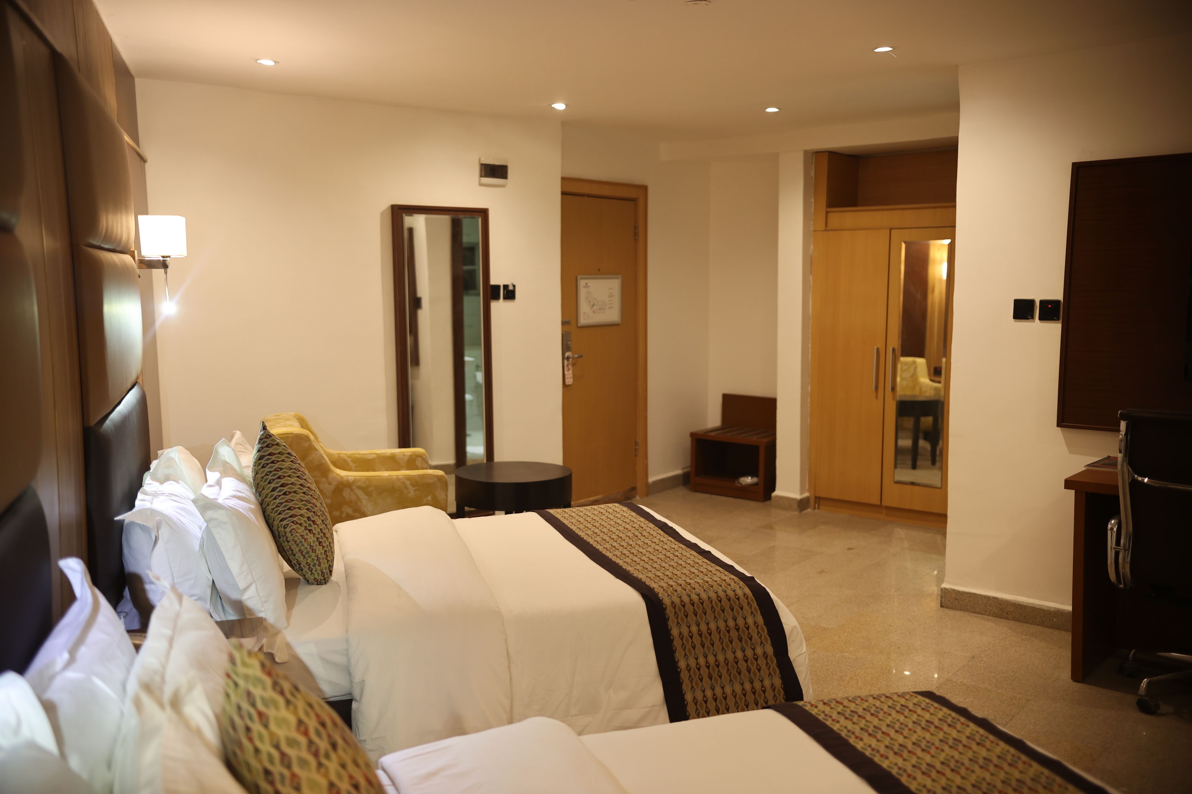 Quarto de hotel com uma cama grande, uma escrivaninha, uma cadeira, um espelho e um guarda-roupa.