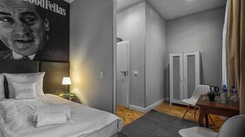 Quarto de hotel com uma cama, mesa de cabeceira com abajur, escrivaninha com cadeiras e guarda-roupa.