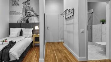 Quarto de hotel moderno com cama, mesa de cabeceira, TV presa na parede e área de chuveiro.