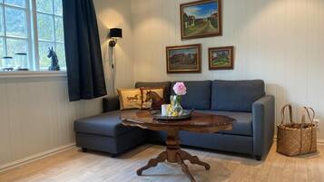 Uma sala de estar com sofá cinza, mesa de centro de madeira com um vaso e bandeja, luminária e quadros nas paredes.