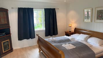 Quarto com cama de madeira, mesa de cabeceira com abajur, janela com cortinas e um armário.