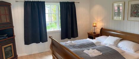 Quarto com cama de madeira, mesa de cabeceira com abajur, janela com cortinas e um armário.