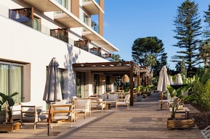 Pátio de hotel com mobiliário para áreas externas, espaço coberto e vista para a fachada do edifício.