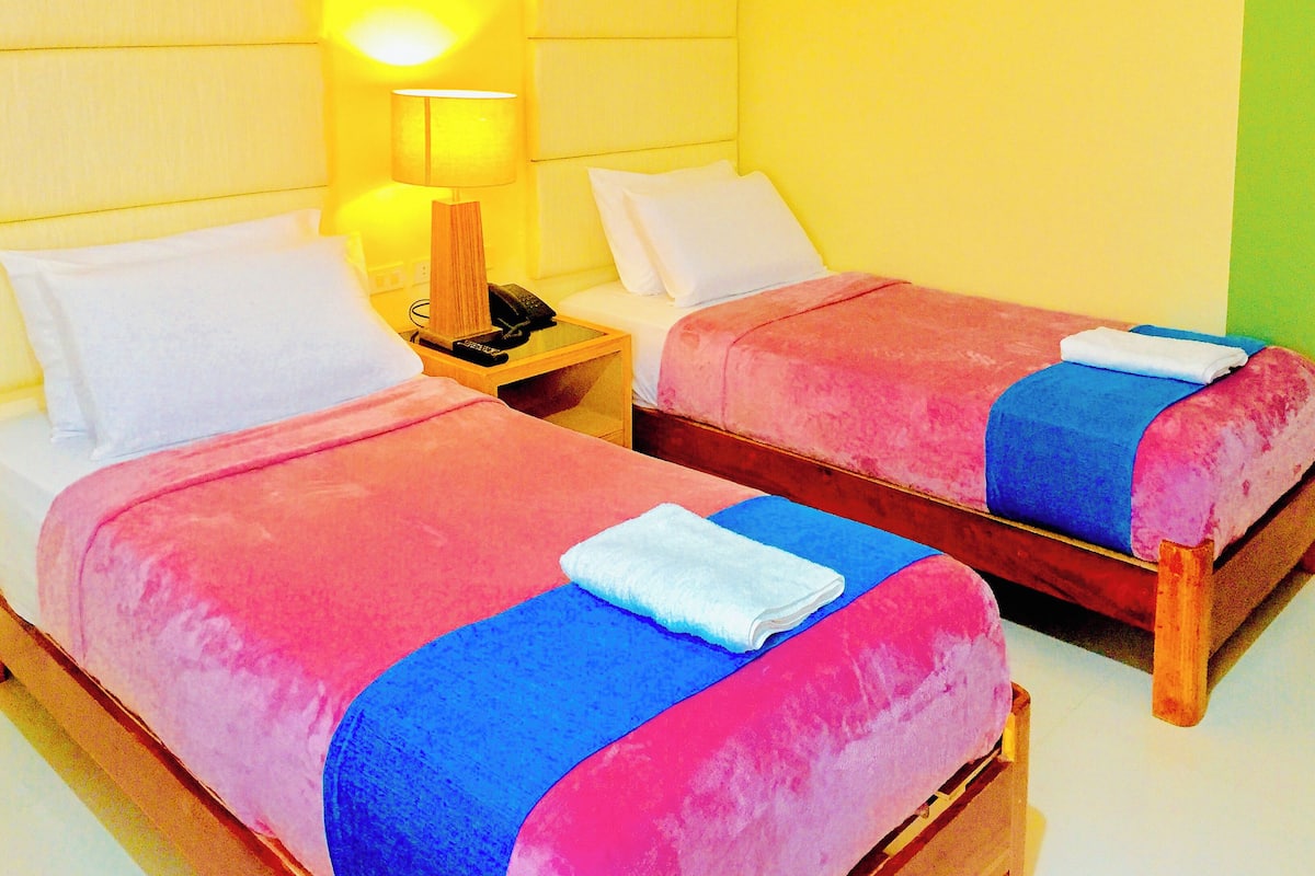 Duas camas com roupa de cama rosa e azul, um abajur e um telefone na mesinha de cabeceira.