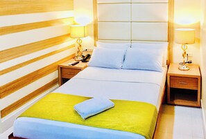 Quarto de hotel com cama, abajures, telefone e mesa de cabeceira de madeira.