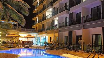 Um hotel com vários andares, piscina, área de estar externa e palmeiras.