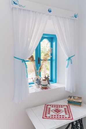Um quarto com janela, uma mesa e um vaso com plantas secas.