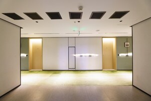Um corredor com parede espelhada, porta iluminada e teto com ventilação.