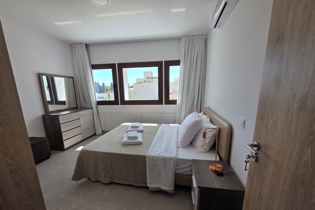 Quarto moderno com cama grande, mesa de cabeceira, cômoda e espelho.