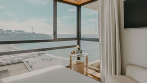 Quarto de hotel com uma janela grande, uma cama, uma mesa pequena com um vaso e uma TV na parede.