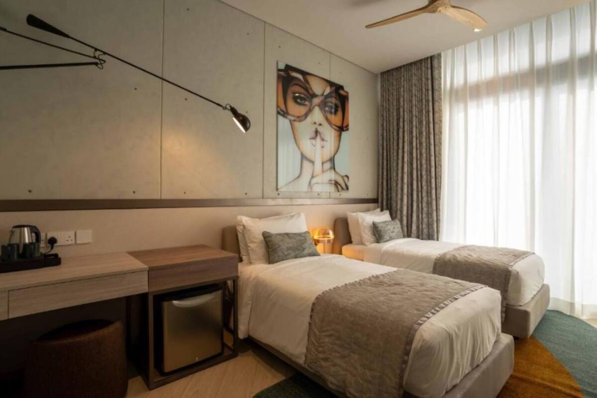 Quarto de hotel com duas camas, uma escrivaninha, máquina de café, luminária na parede e um quadro.
