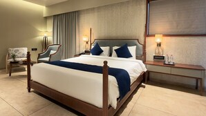 Quarto de hotel com uma cama grande, mesas de cabeceira, uma cadeira e uma escrivaninha.