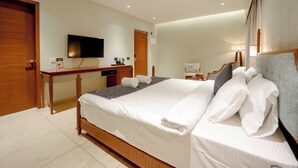 Quarto bem iluminado com uma cama grande, uma televisão de tela plana na parede, uma escrivaninha com cadeira e uma porta.