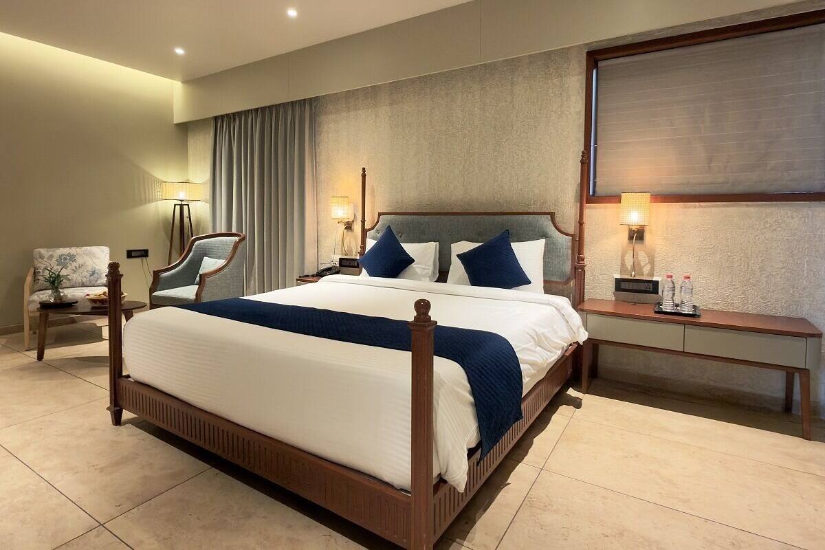 Quarto de hotel com uma cama grande, mesas de cabeceira, uma cadeira e uma escrivaninha.