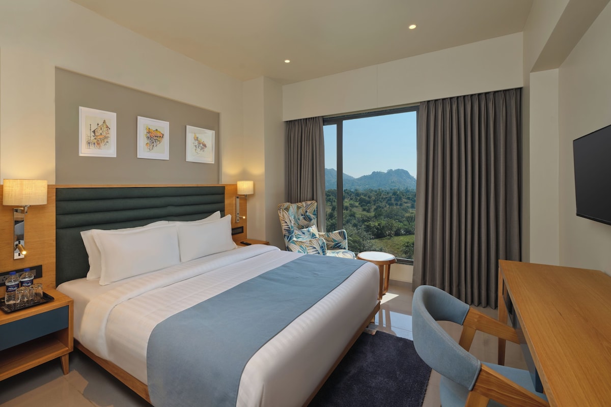 Quarto de hotel com uma cama grande, uma escrivaninha, uma cadeira e vista para as montanhas.