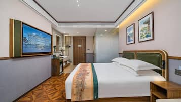 Quarto de hotel com cama, escrivaninha, cadeira, espelho e televisão na parede.
