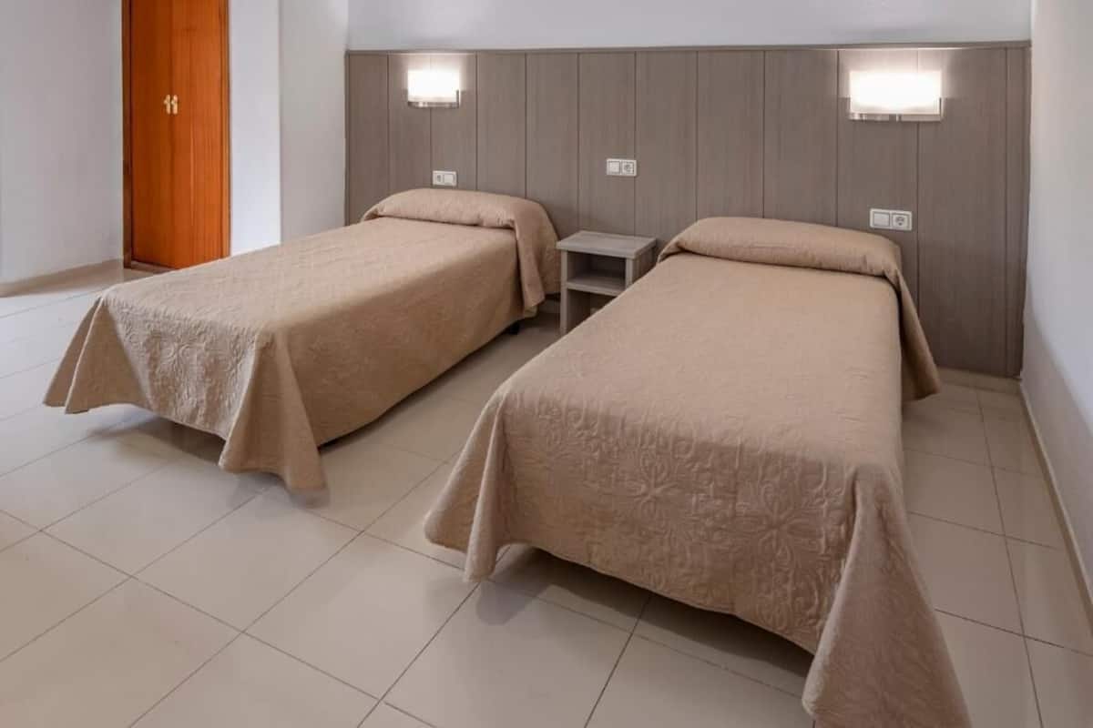 Quarto de hotel com duas camas, uma porta de madeira e luminárias fixadas na parede.