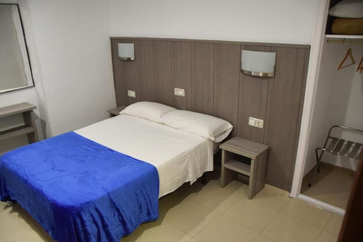 Uma cama de solteiro com colcha azul, cabeceira de madeira, mesas de cabeceira e um espelho.