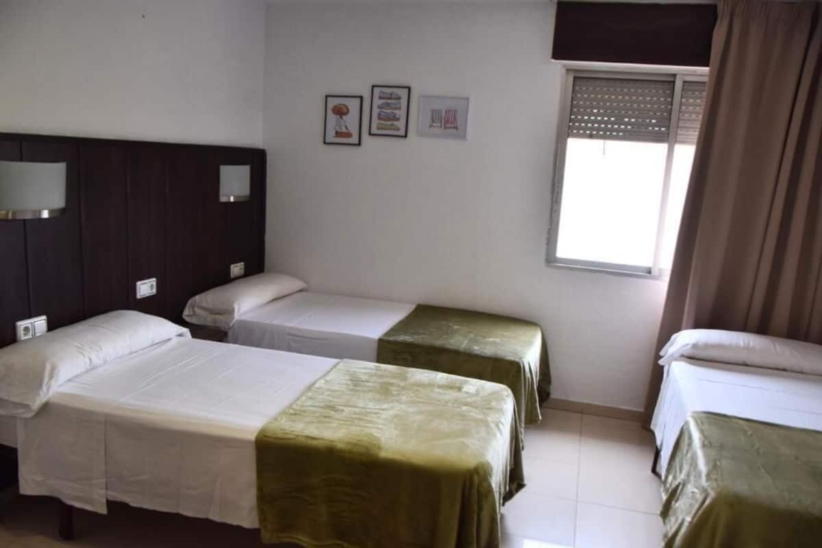Quarto de hotel com duas camas de solteiro, uma janela com persianas e três quadros na parede.