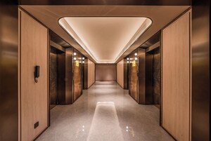 Um hall de elevadores moderno com piso polido, painéis de madeira e luminárias no teto.