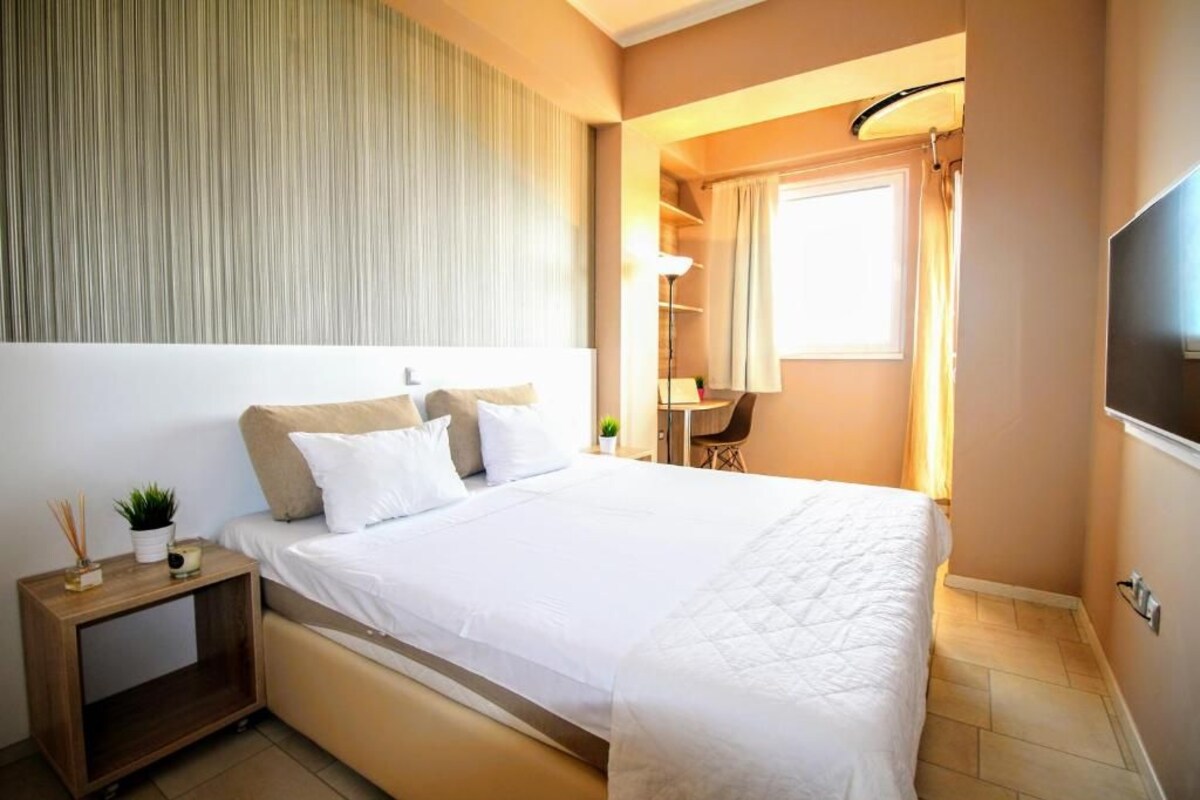 Quarto de hotel com cama, mesa de cabeceira, abajur e televisão.