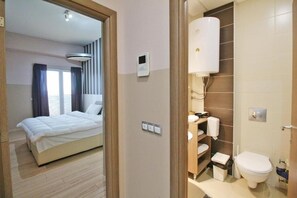 Quarto de hotel com cama, banheiro com vaso sanitário e chuveiro.