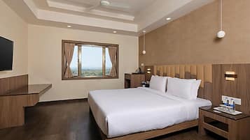 Quarto de hotel com cama, mesas de cabeceira, televisão, janela com cortinas, ventilador de teto e vista para o exterior.