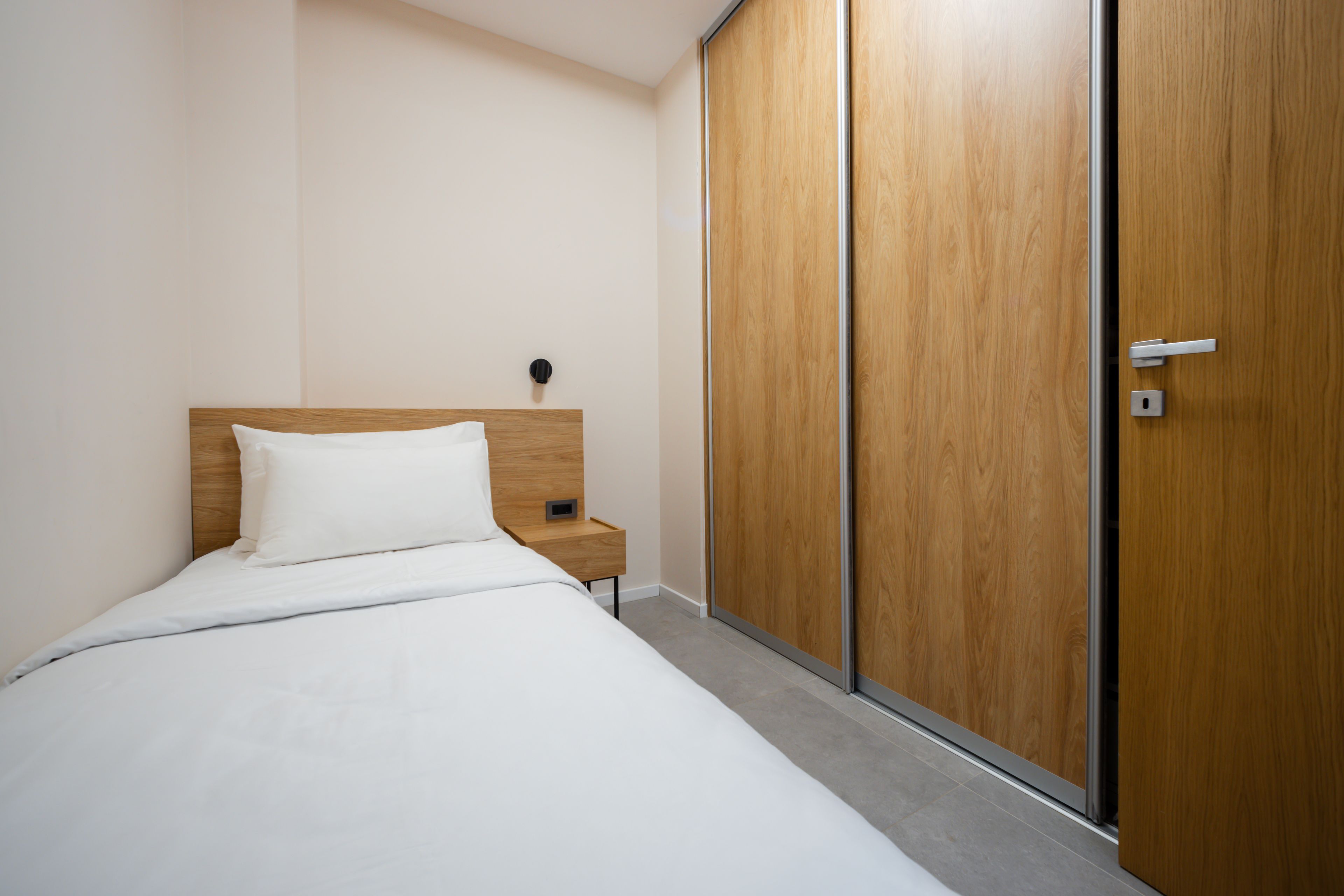 Quarto com cama, guarda-roupa de madeira e mesa de cabeceira.