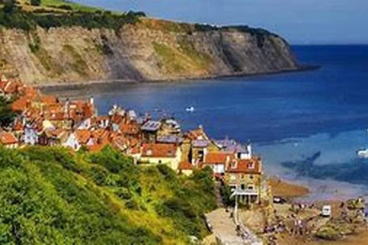 Uma vila costeira com edifícios ao longo do penhasco, uma praia e barcos na água.