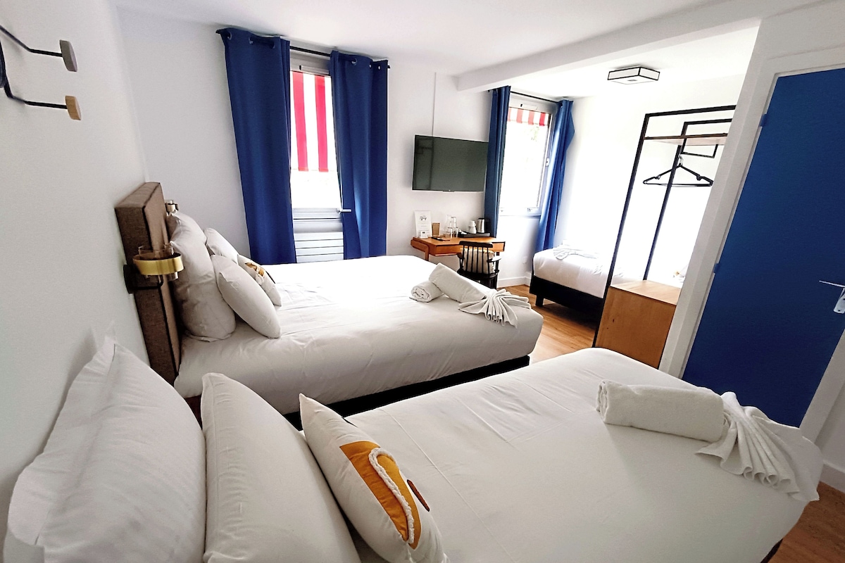 Quarto de hotel com duas camas, televisão, escrivaninha e banheiro visível por uma porta aberta.
