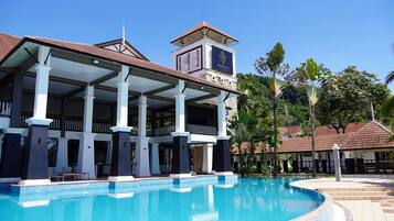 Um hotel com piscina, área coberta e torre com relógio.