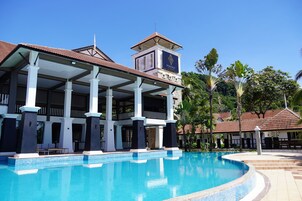 Um hotel com piscina, área coberta e torre com relógio.