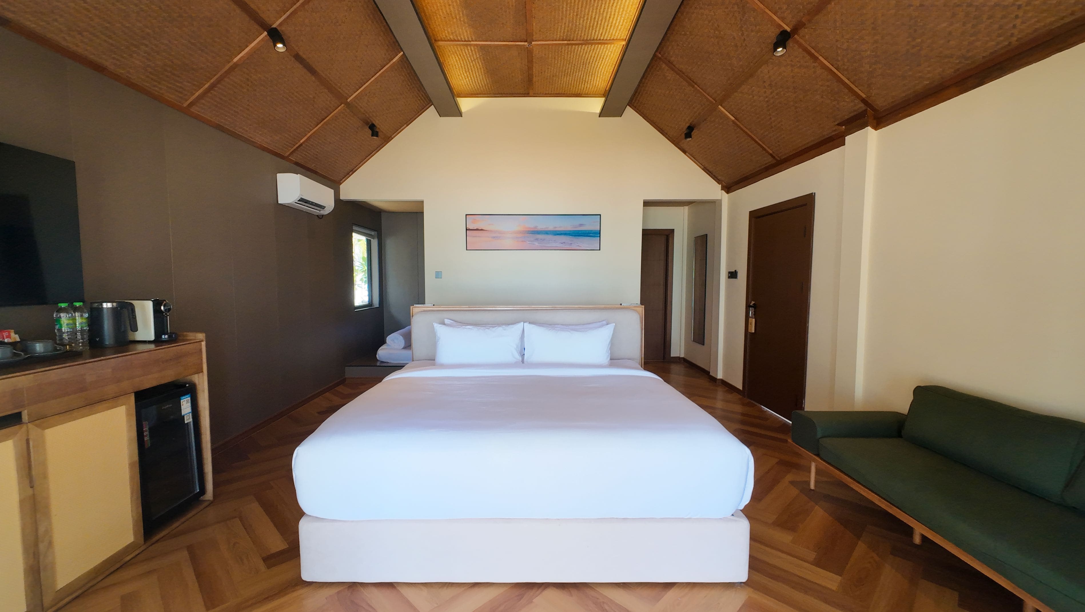 Um quarto espaçoso com uma cama grande, teto de madeira, pequeno espaço de cozinha e um sofá verde.