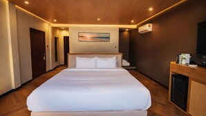 Quarto de hotel com uma cama grande, uma mesa de trabalho com televisão e um quadro na parede.