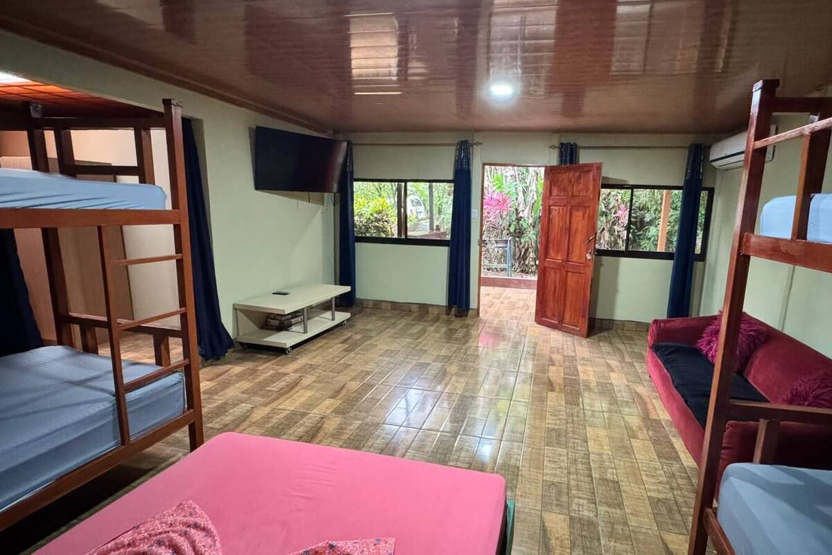 Um quarto de dormitório com beliches, escrivaninha, televisão e janela com cortinas.