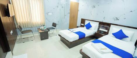 Quarto de hotel com duas camas, uma escrivaninha, uma cadeira e um ar condicionado.