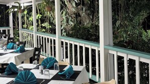 Restaurante com mesas preparadas para refeições, teto branco e corrimão verde.
