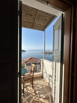 Uma porta aberta dá para uma varanda com vista para o mar e piso de azulejos.