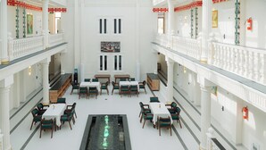 Um saguão de hotel com um recurso central de água, várias áreas de refeições e um átrio com pé-direito alto.
