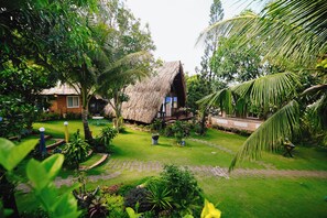 Casa com telhado de palha, cercada por vegetação exuberante e um jardim bem cuidado.