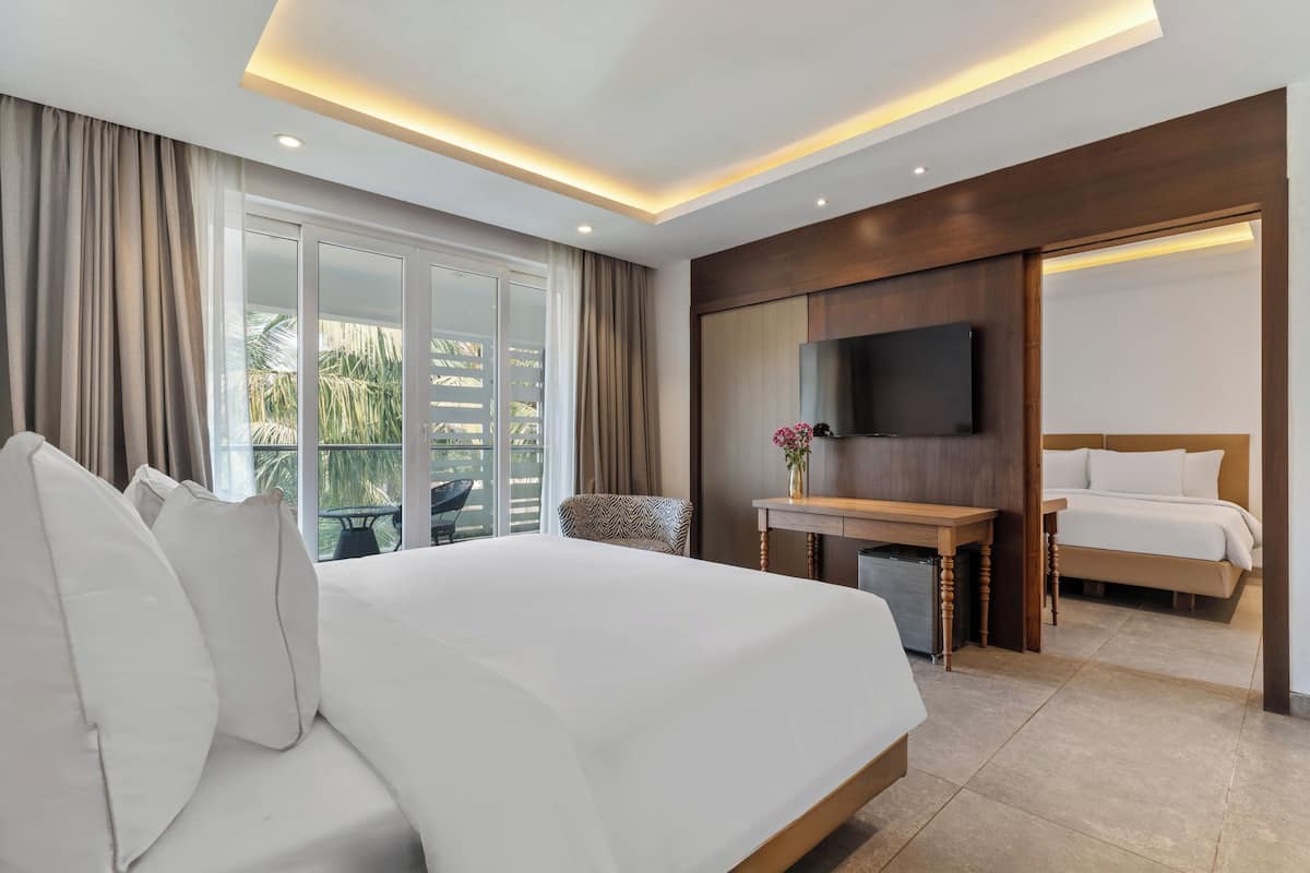 Quarto de hotel com uma cama grande, uma escrivaninha com televisão de tela plana e uma varanda com cortinas.