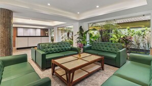 Uma sala de estar moderna com sofás verdes, uma mesa de centro de madeira e uma cozinha ao fundo.