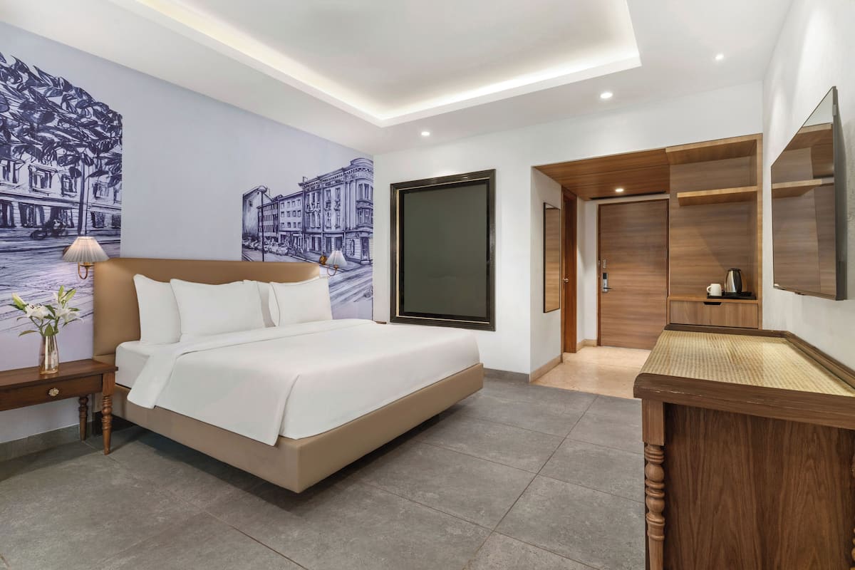 Quarto de hotel moderno com uma cama grande, uma escrivaninha, um guarda-roupa e uma televisão montada na parede.