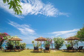 Um espaço de relaxamento à beira-mar, com toldos de palha e espreguiçadeiras de madeira voltadas para o mar.