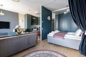 Quarto de hotel moderno com sofá, cama, televisão e área de cozinha.