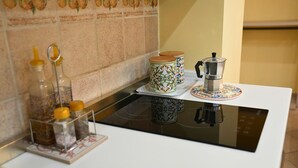 Cozinha com bancada branca, fogão e objetos decorativos, incluindo uma cafeteira e xícaras estampadas.