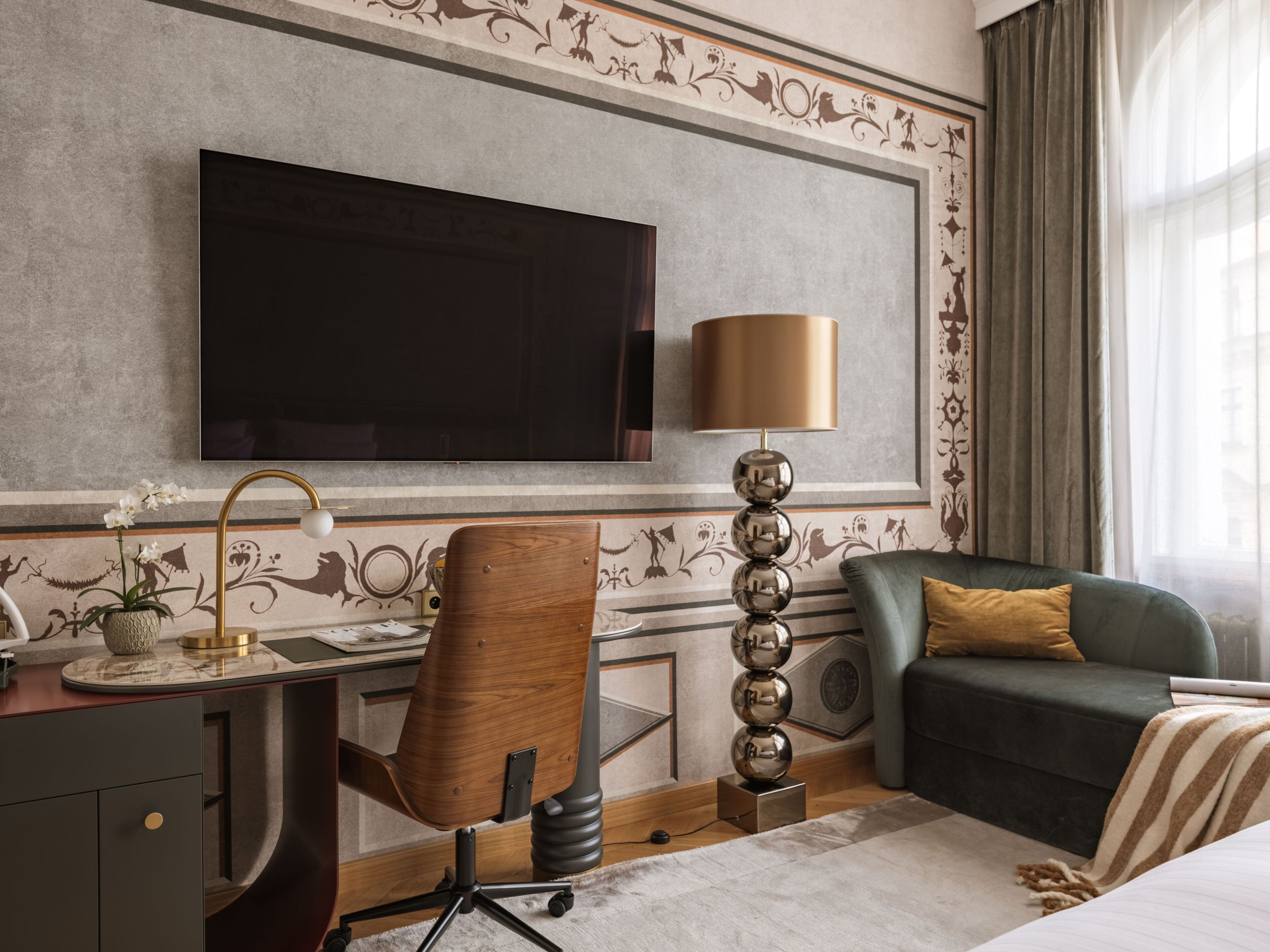 Quarto de hotel com televisão de tela plana, uma escrivaninha com cadeira, sofá, abajur e um painel decorativo na parede.