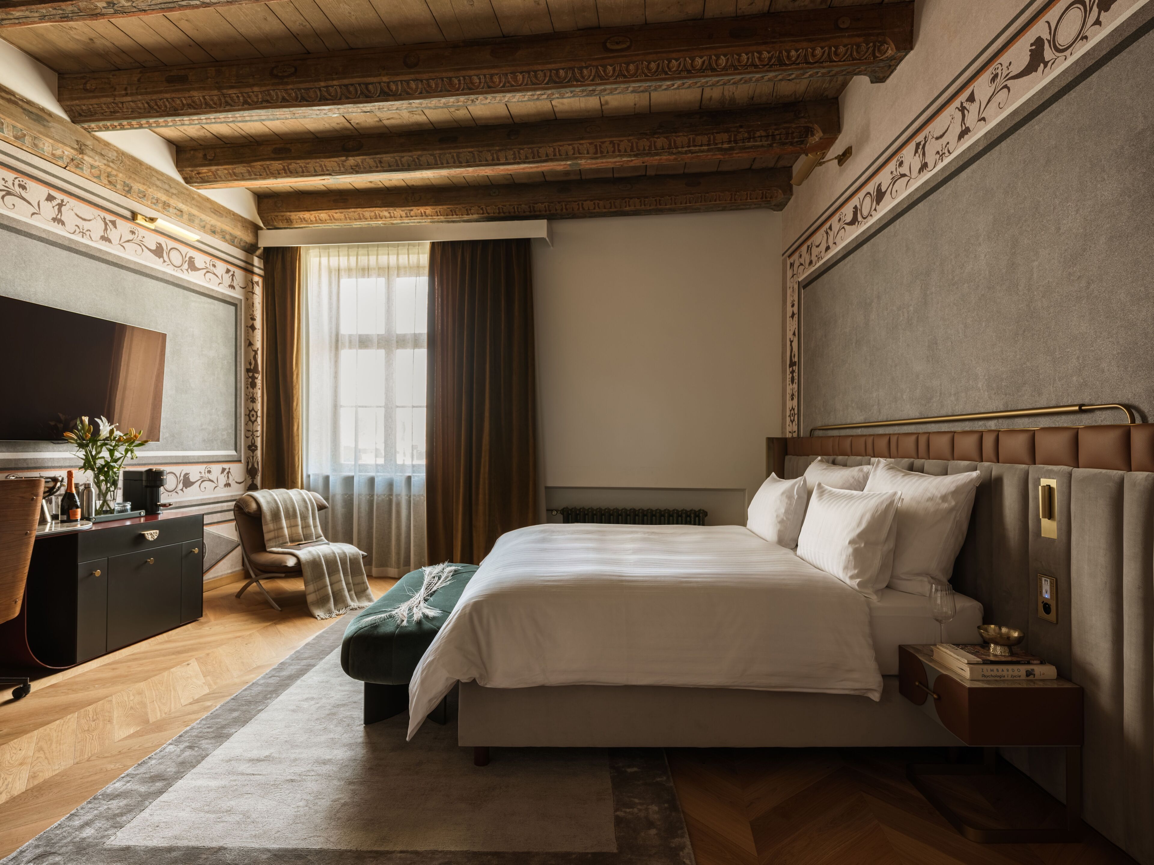 Quarto com cama grande, escrivaninha, cadeira, televisão e janela com cortinas.