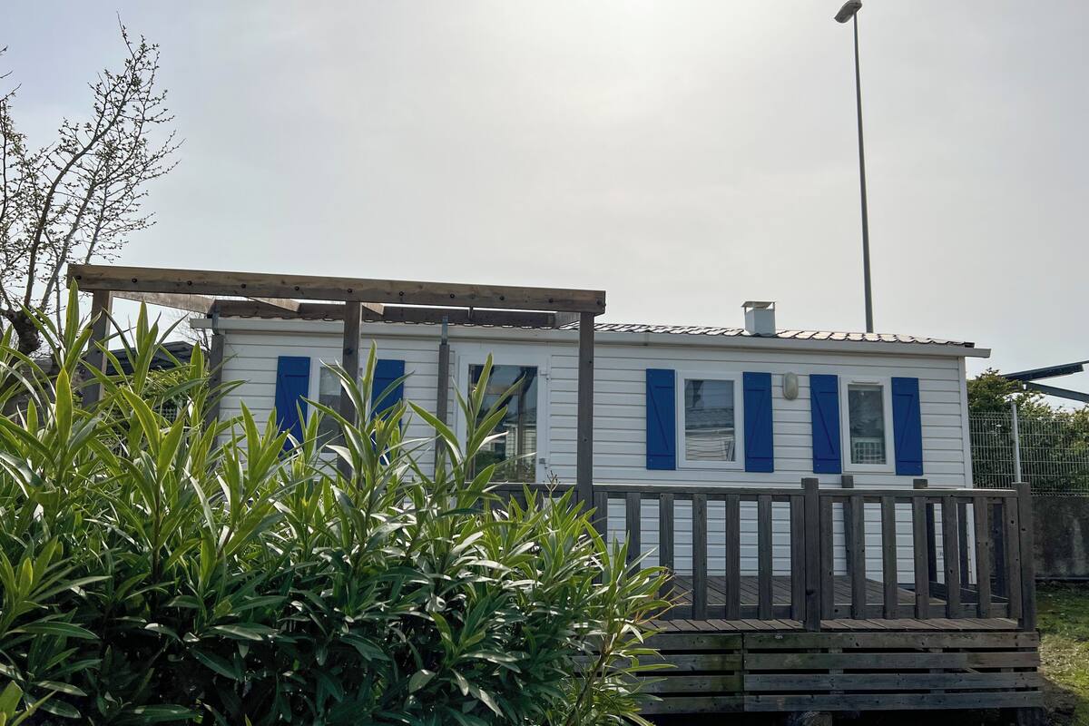 Um pequeno edifício térreo com deck de madeira e persianas azuis.