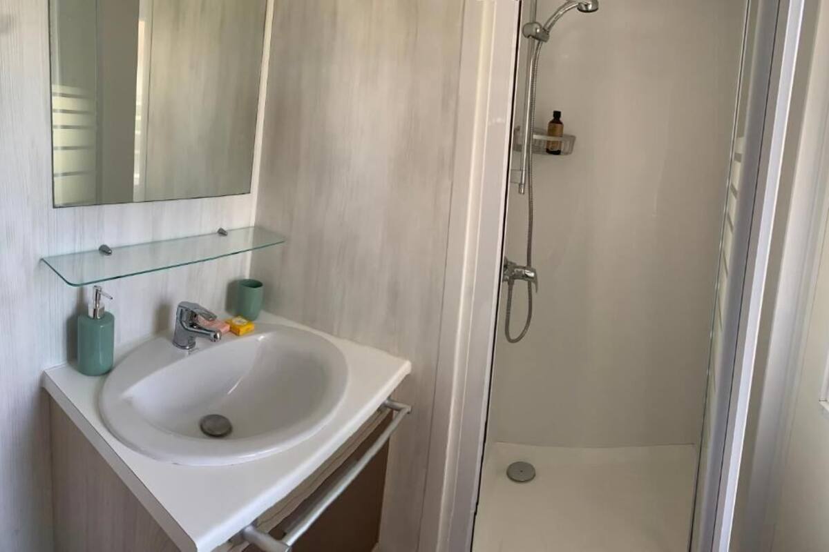 Casa de banho com uma pia branca, uma prateleira de vidro, um espelho e um chuveiro.